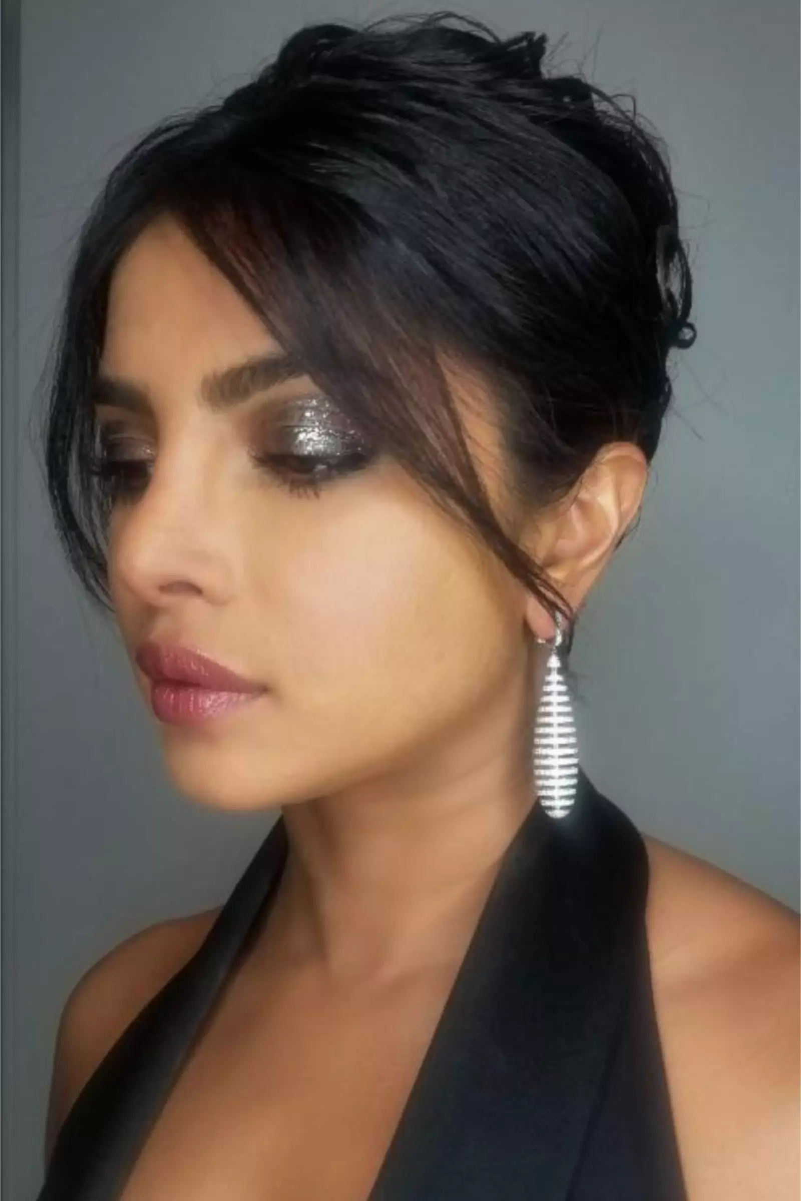 Pictiúr den aisteoir Priyanka Chopra atá ag caitheamh a cuid gruaige suas i gcarn agus a súile clúdaithe le gliondar péatardhathanna