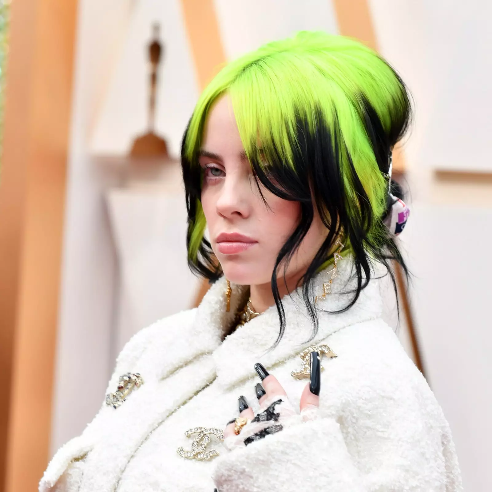 Billie Eilish gade sou kote ak cheve nwa ak lumineuz vèt rale nan yon pen ki ba ak moso nan cheve ankadre figi l '.