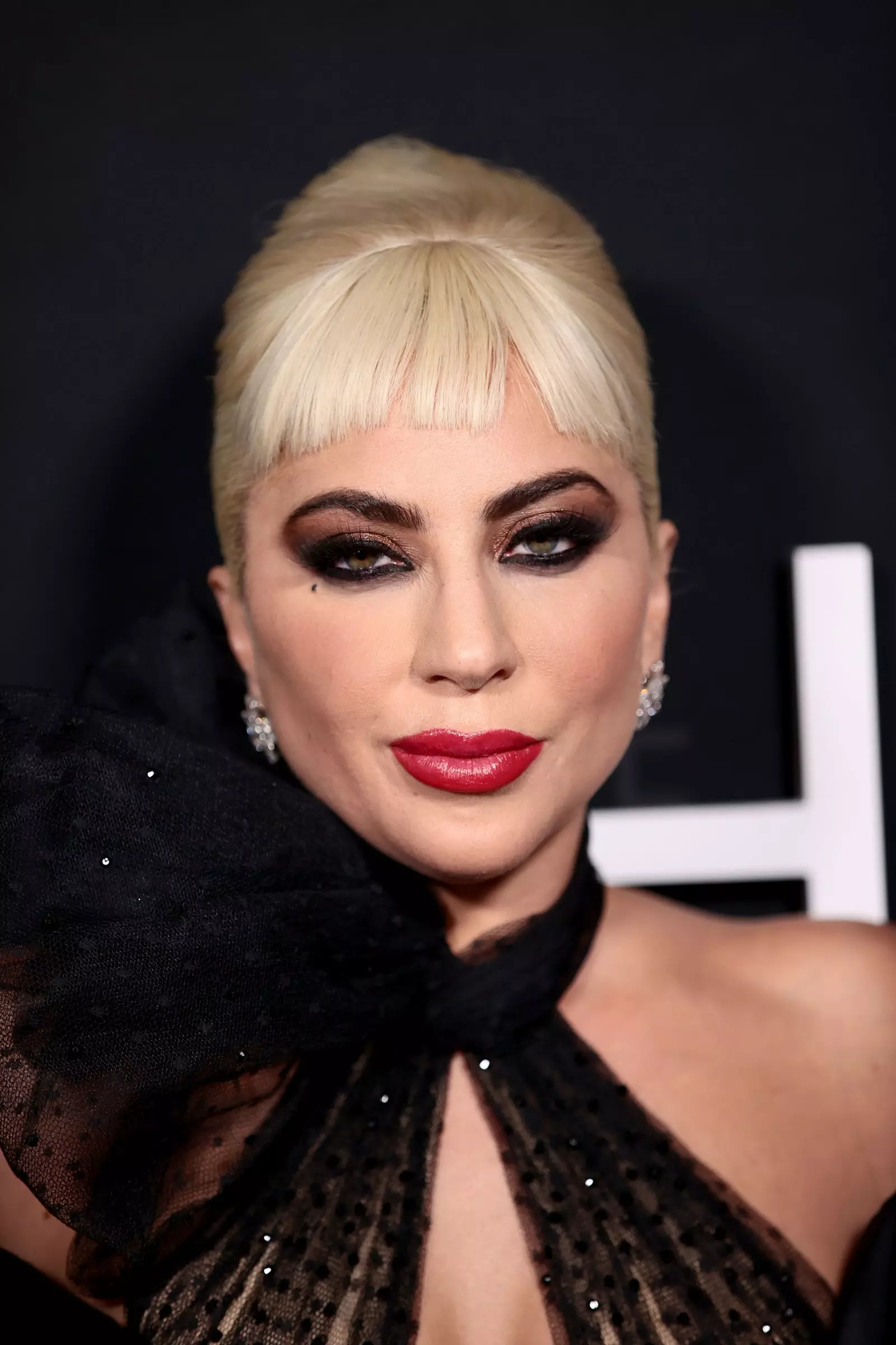 Lady Gaga wọ bleached bilondi updo pẹlu omo bangs kan smokey oju ati pupa aaye fun Ile ti Gucci New York Premiere.