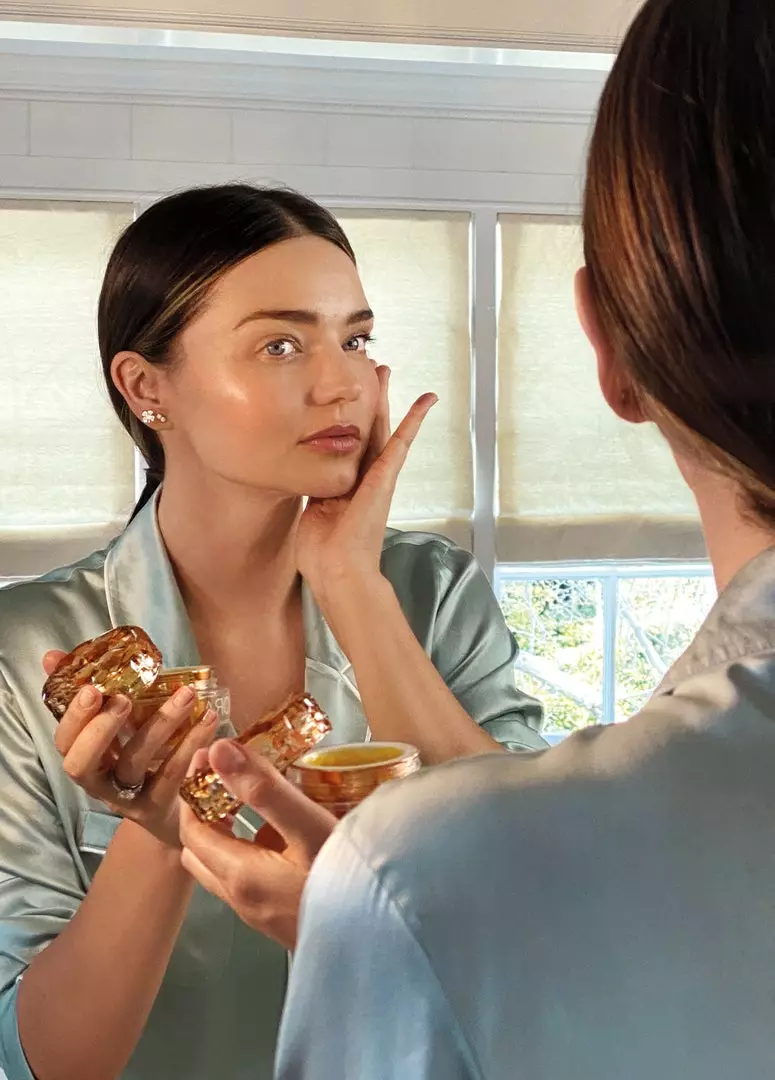 Si Miranda Kerr sa bahay ay nakasuot ng robe sa bahay, buhok sa likod, naglalagay ng produkto ng skincare