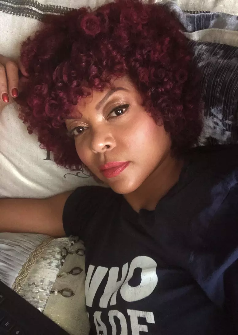 Eserese nke onye na-eme ihe nkiri Taraji P. Henson n'ụlọ yi uwe t-shirt, curls eke, na lipstick na-acha uhie uhie.