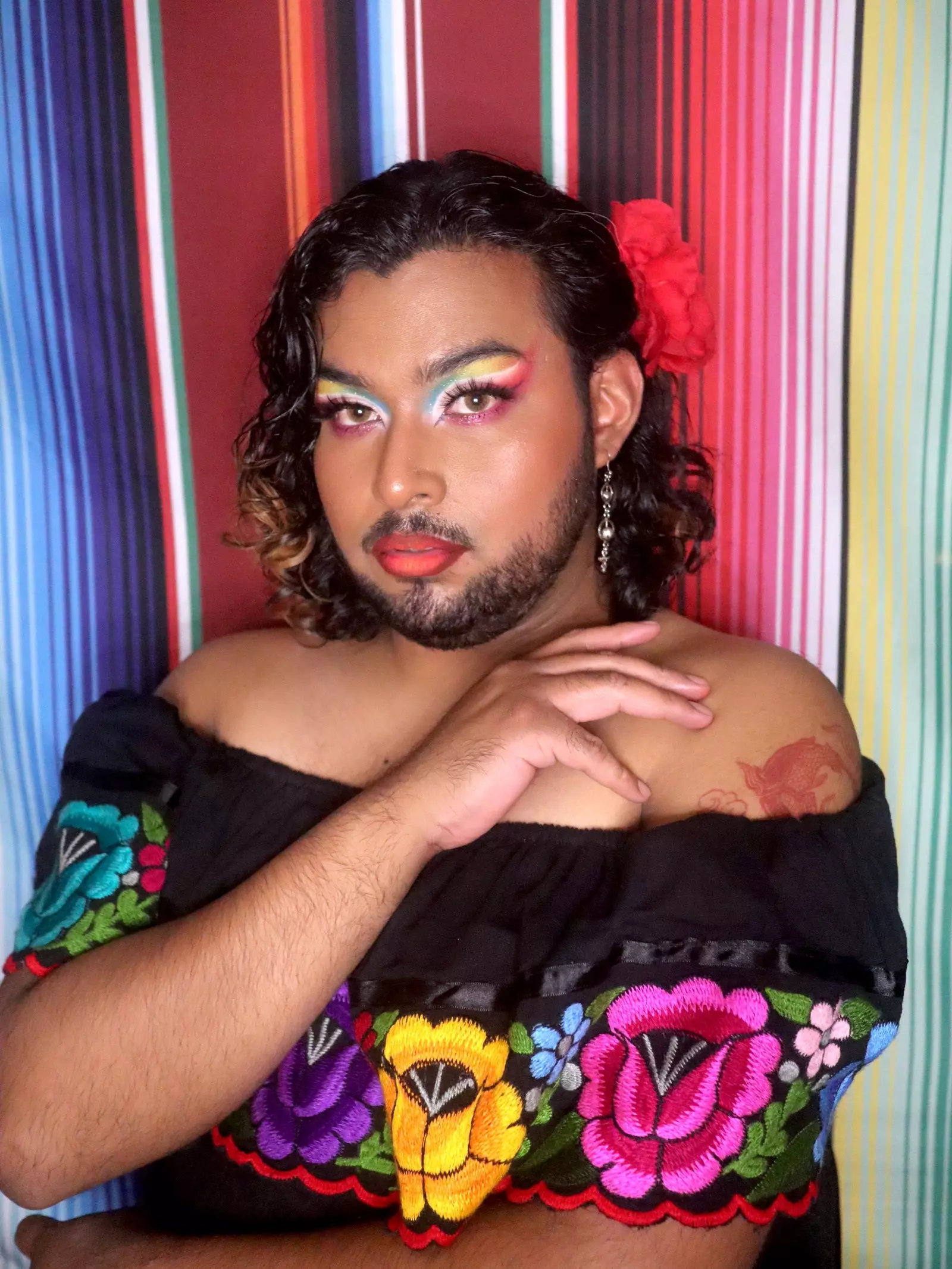 Hulagway sa dili binary influencer ang makeupmariachi nga nagsul-ob og itom sa abaga nga binordahan nga sinina ug kolor nga makeup