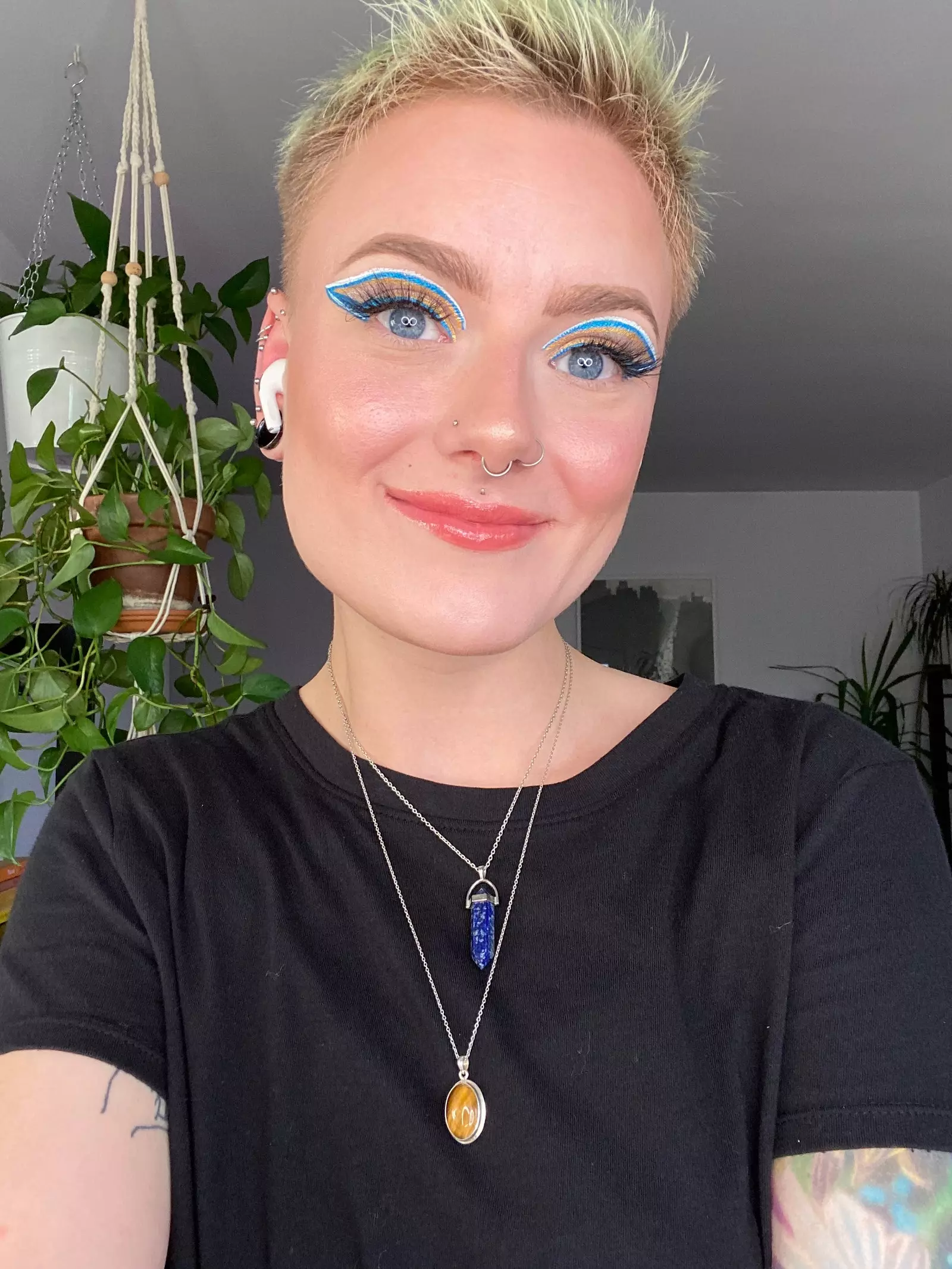 selfie of non binér influencer deesikoramua dina kaos oblong hideung. aranjeunna gaduh eyeliner grafis biru sareng bodas.