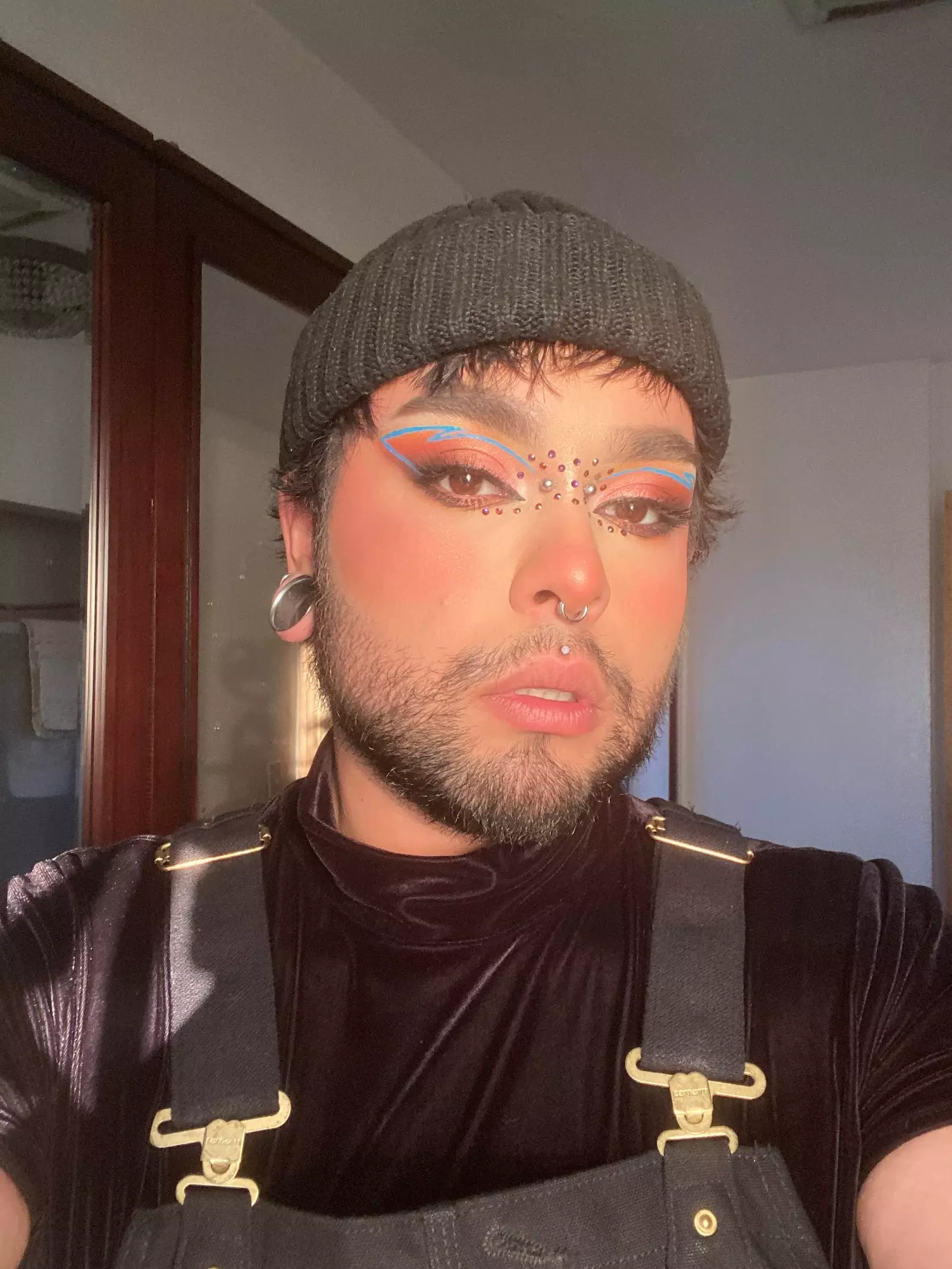 selfie sa dili binary beauty influencer realsickpuppy nga nagsul-ob og dramatikong asul ug pink nga makeup sa mata usa ka gray nga beanie ug itom...